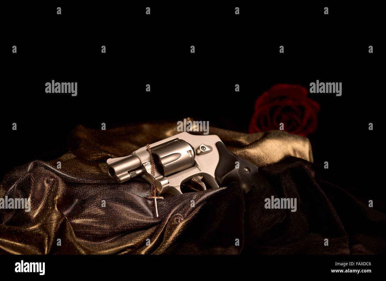 Snubnose 38 revolver laying across gold satin with a gold cross and ...