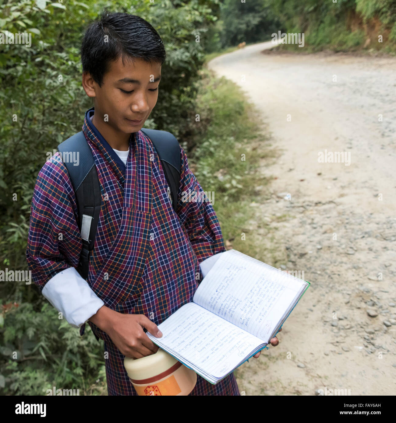 A boy with a checkered robe carrying a backpack and reading a book on ...