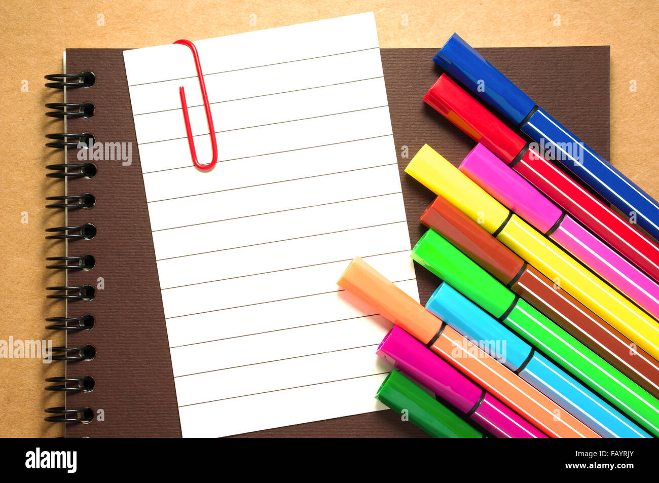 Note paper clip on notebook with colorful markers on brown cardboard ...