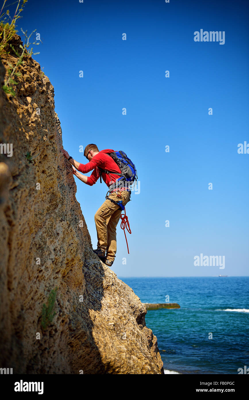 young man climbing up the rock on sea background Stock Photo - Alamy