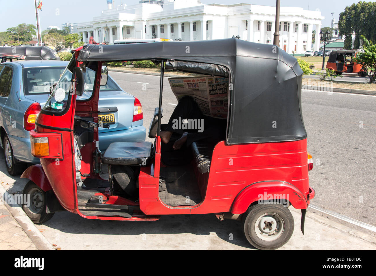 A tut-tut driver reading his newspaper in his parked three-wheeler as ...