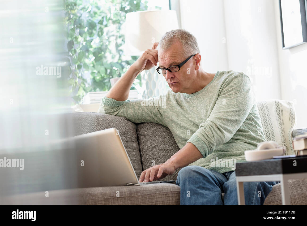 Man sitting on sofa using laptop at home Stock Photo - Alamy