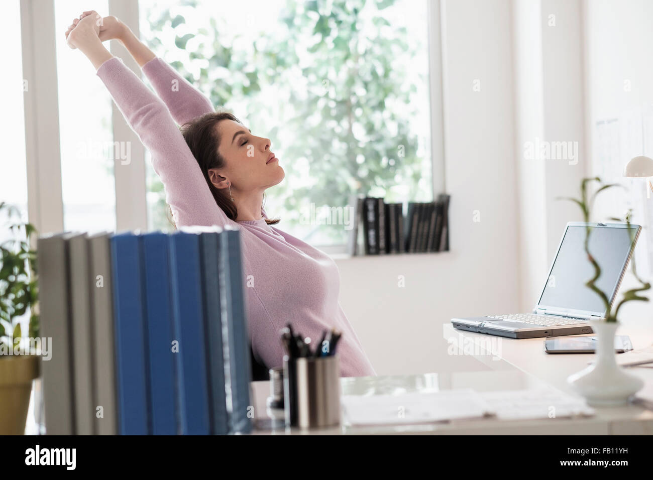 Young woman stretching by desk Stock Photo - Alamy