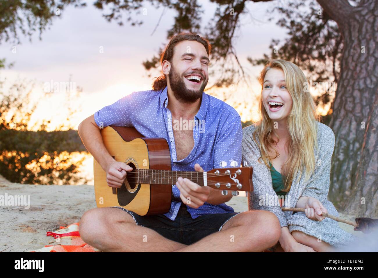 Young couple playing guitar by lake Stock Photo - Alamy