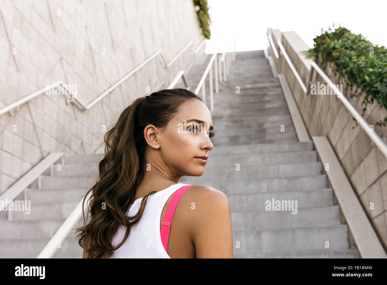 Low angle rear view of young woman at the bottom of stairway looking ...