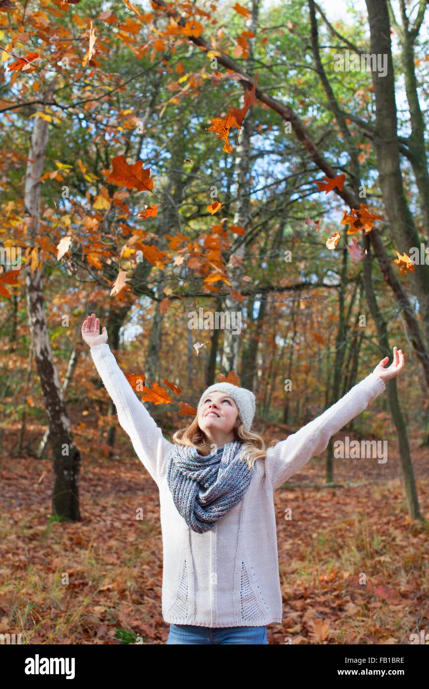 Teenage girl in forest arms raised throwing autumn leaves, looking up ...