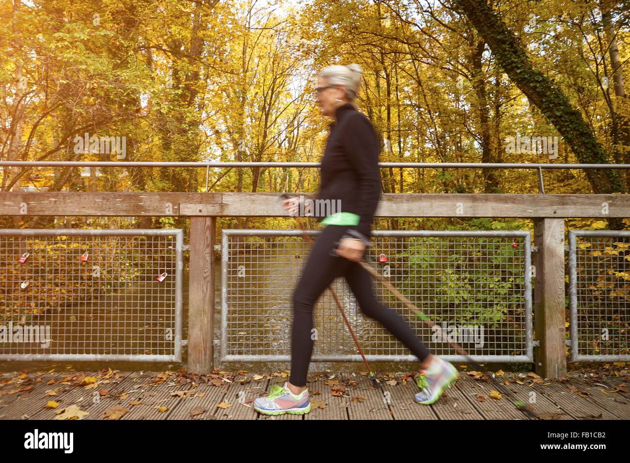 Senior female nordic walker striding over park footbridge Stock Photo ...