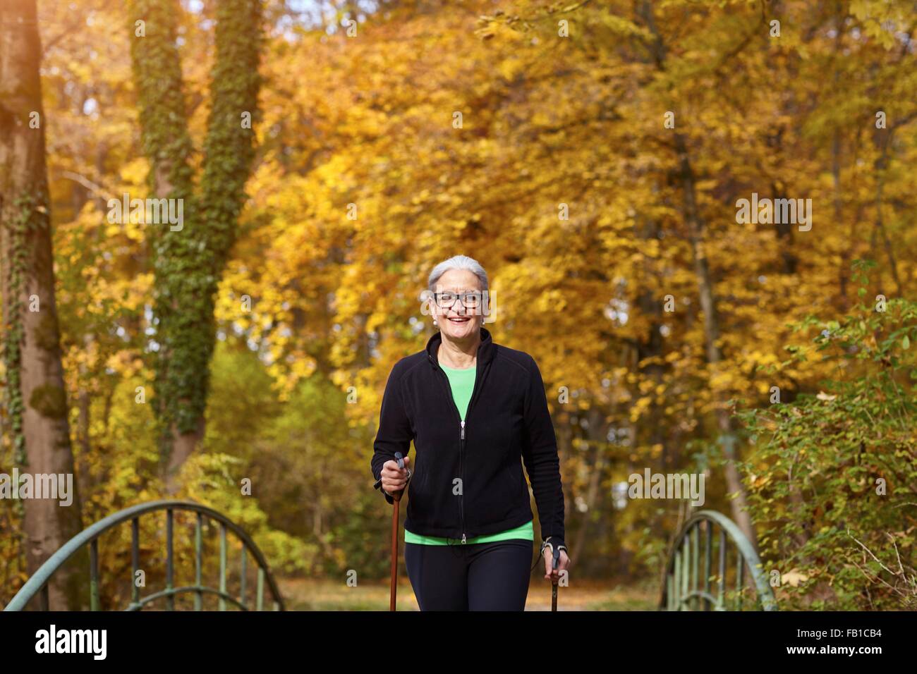 Senior female nordic walker crossing footbridge in autumn park Stock ...