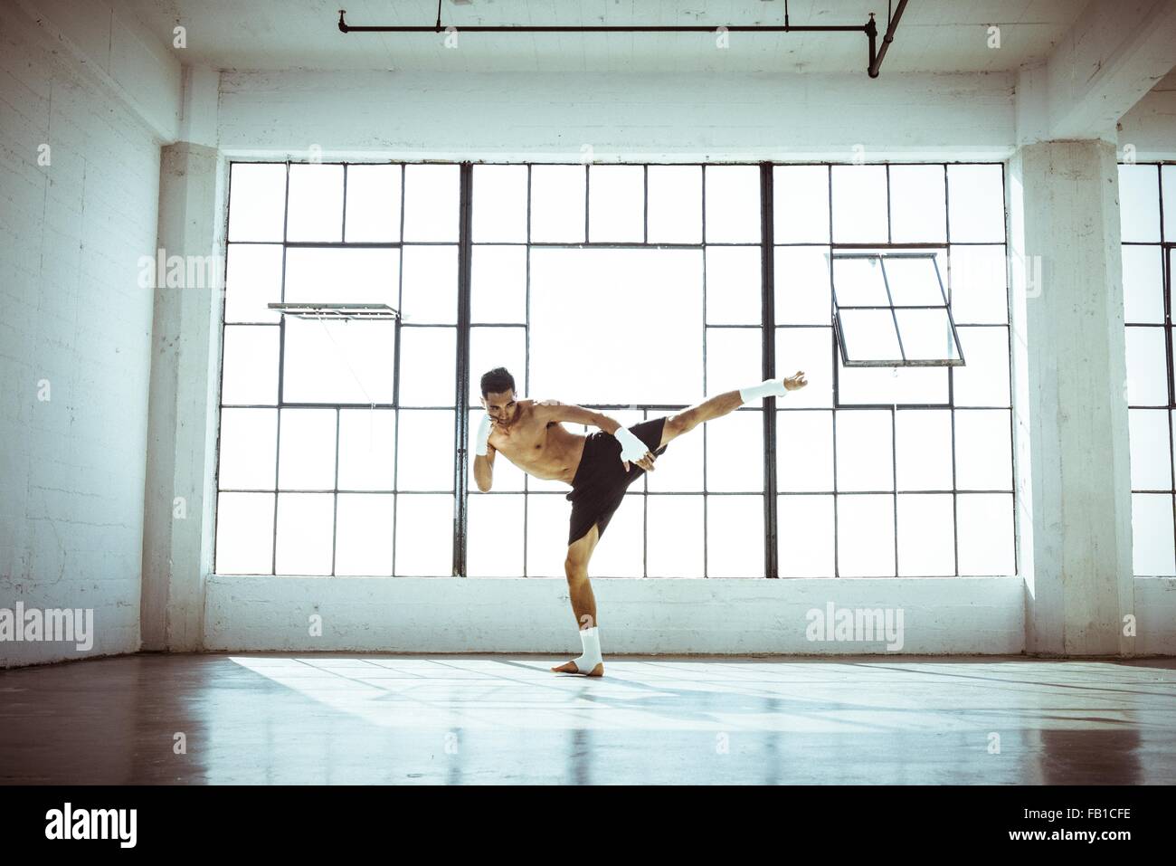 Full length front view of young man in gym leg raised in kickboxing ...