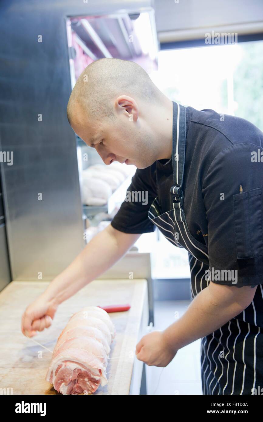 Young butcher tying meat joint in butchers shop Stock Photo - Alamy