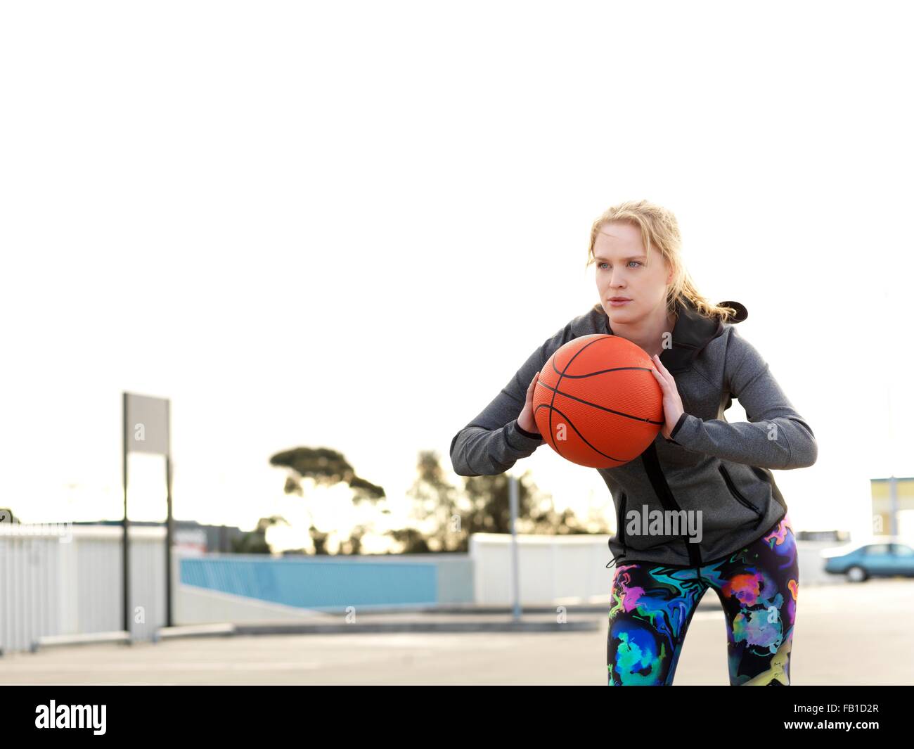 Portrait of young female basketball player practicing throw in parking ...
