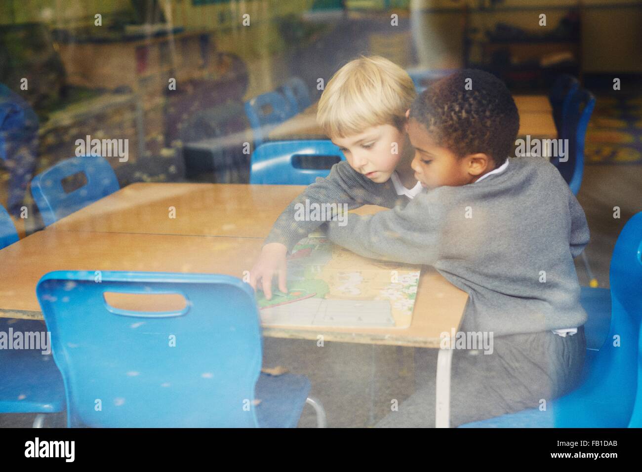 Window view of two boys doing puzzle at desk in elementary school ...