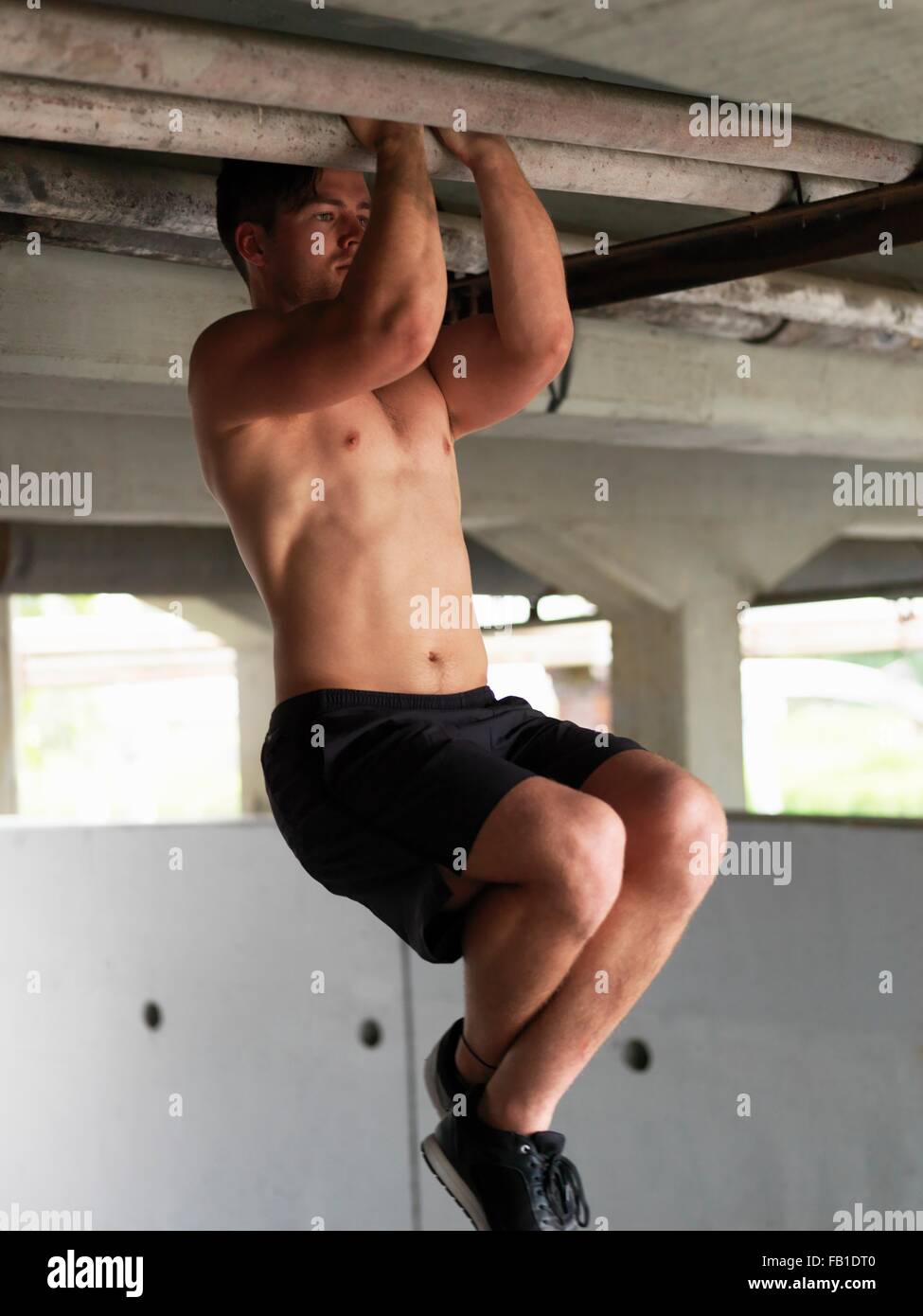 Young man doing pull ups under bridge Stock Photo - Alamy