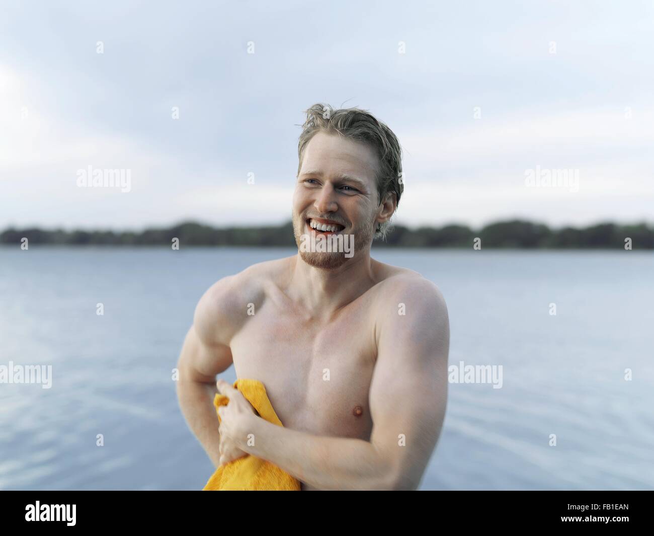 Bare chested young man drying off with towel, looking away smiling ...