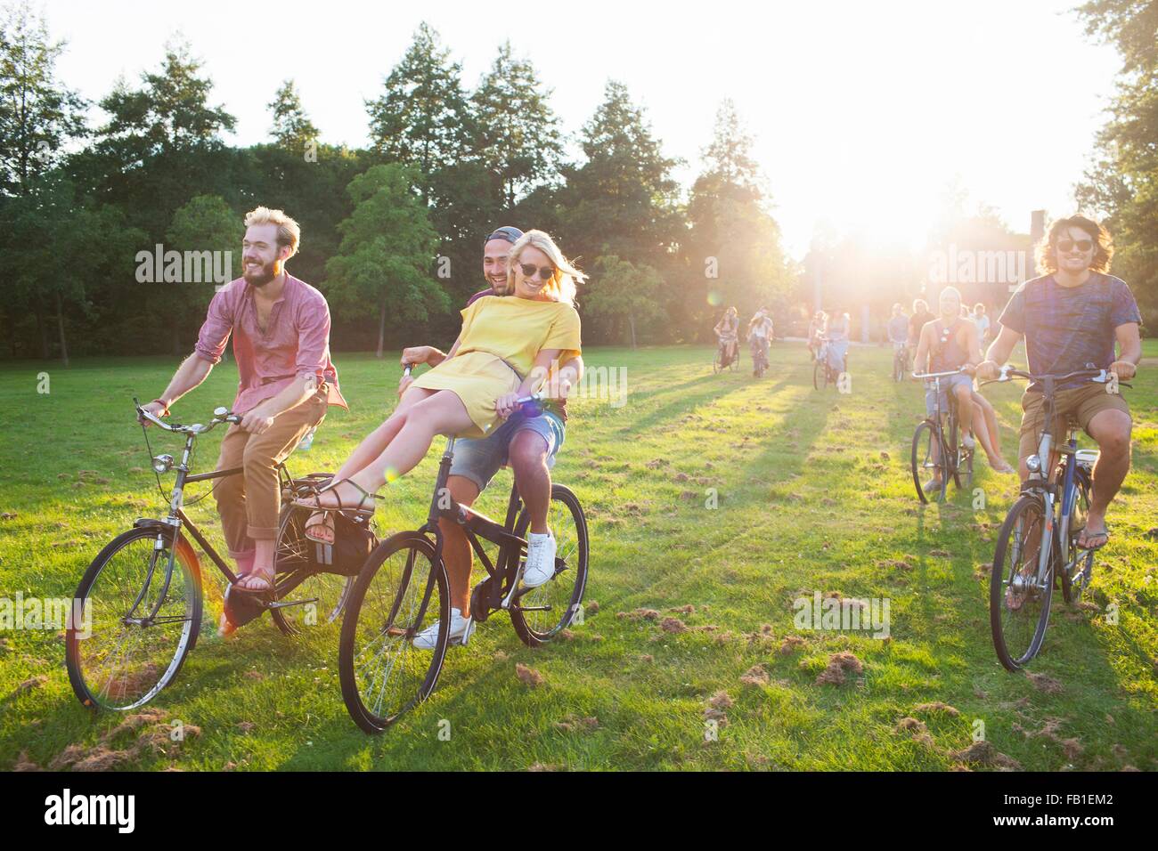 Crowd of partygoing adults arriving on bicycles to sunset park party ...