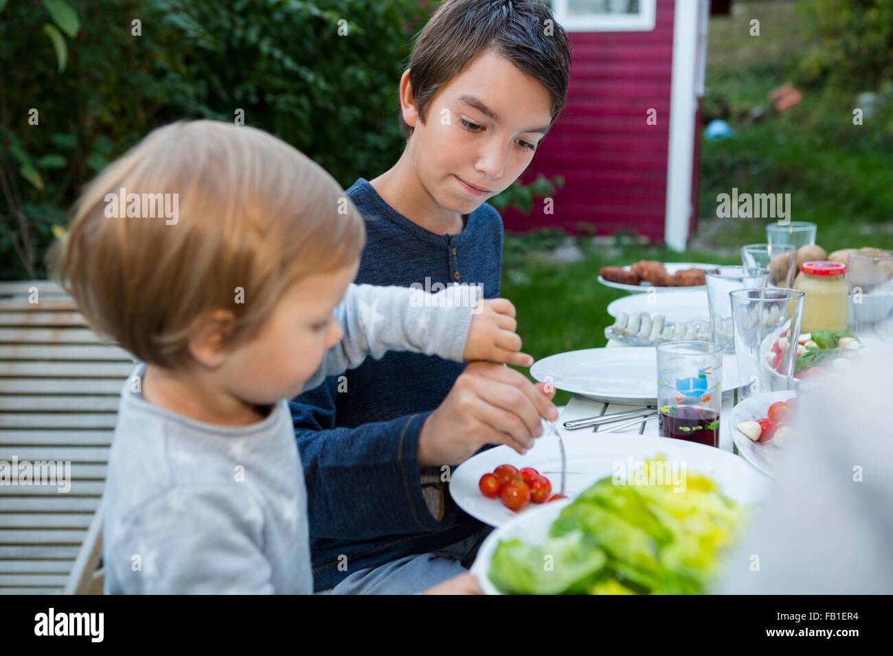 Teenage boy helping female toddler eat food at garden barbecue Stock ... Teenage boy helping female toddler eat food at garden barbecue Stock ...