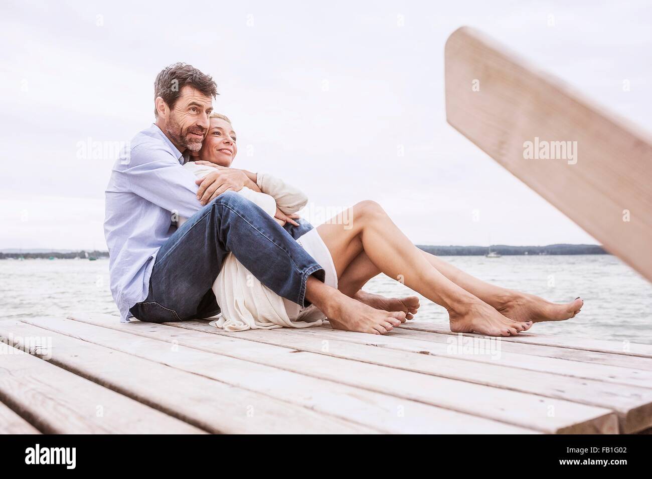 Mature couple sitting, hugging, on pier Stock Photo - Alamy