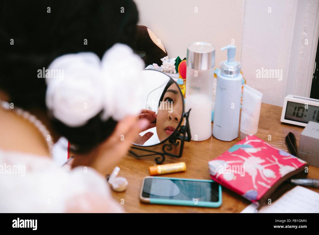 Over the shoulder view of young woman at dressing table applying makeup ...