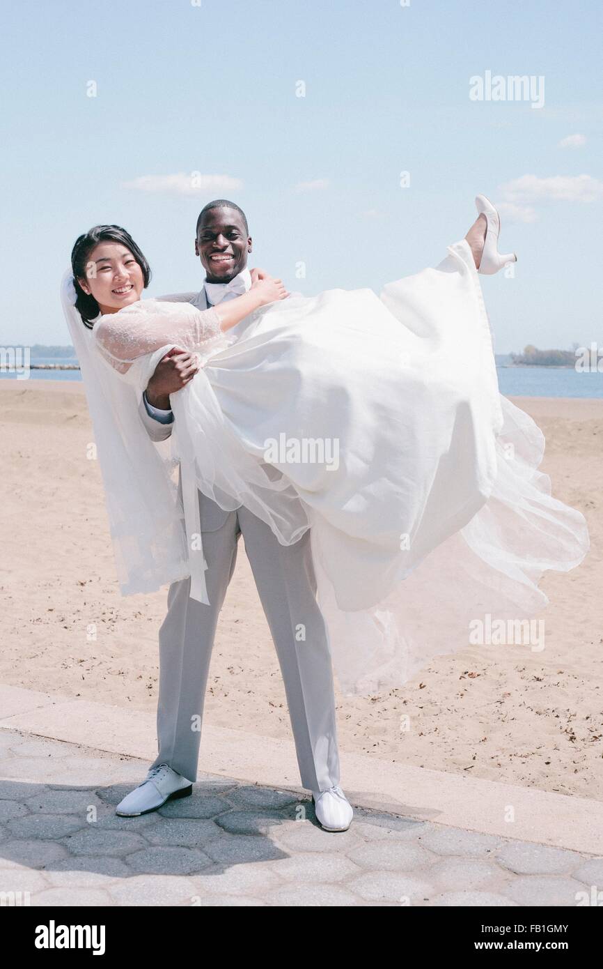 Bridegroom on beach carrying bride looking at camera smiling Stock ...