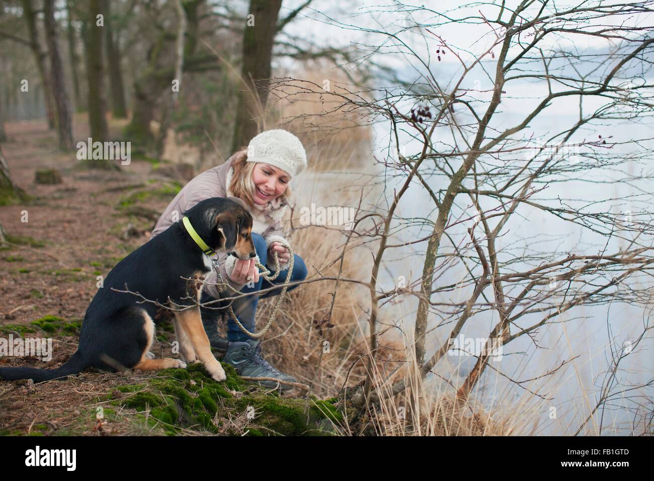 Mid adult woman crouching with her dog on riverbank Stock Photo - Alamy