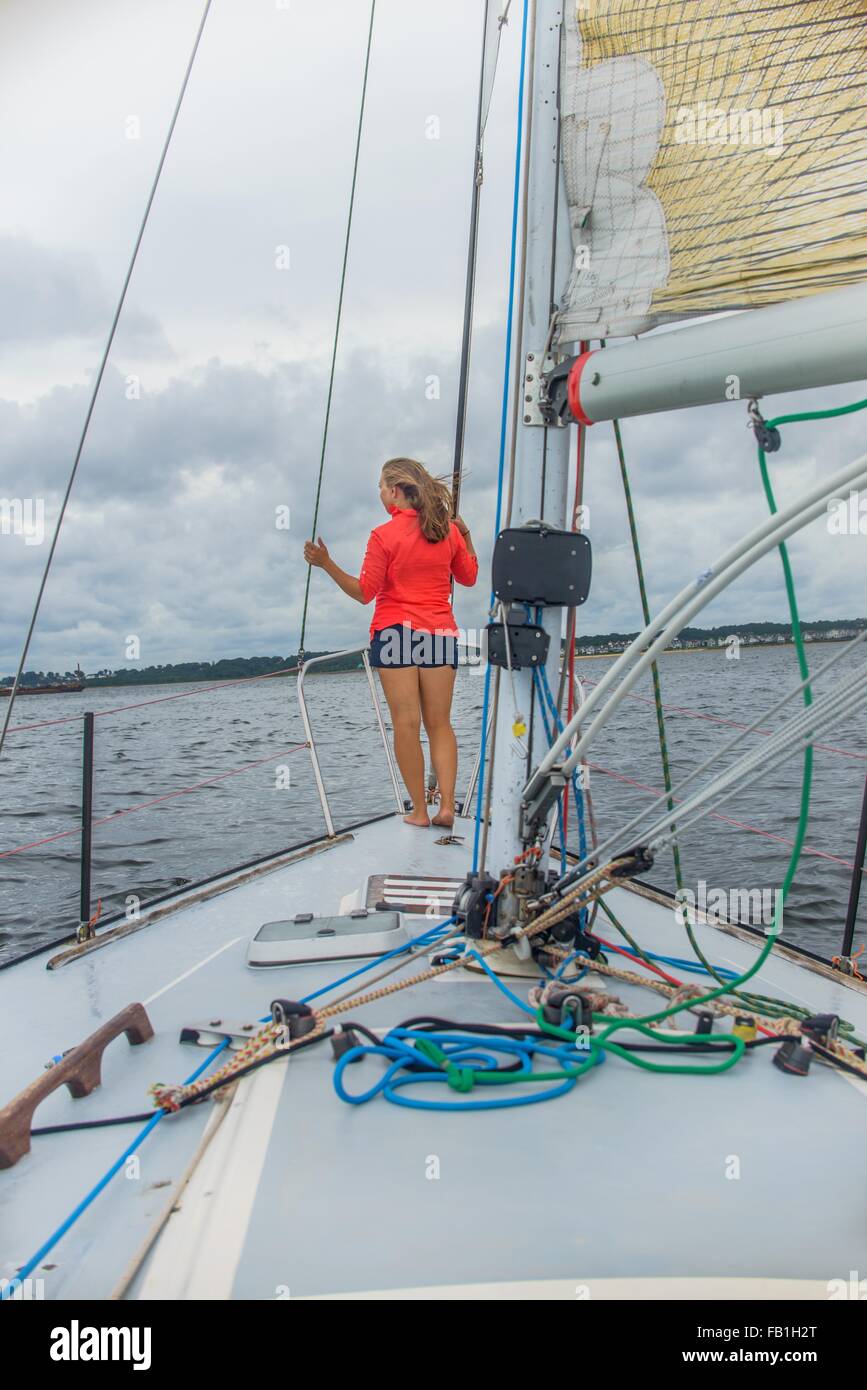Full length rear view of young woman on bow of sailboat looking away ...