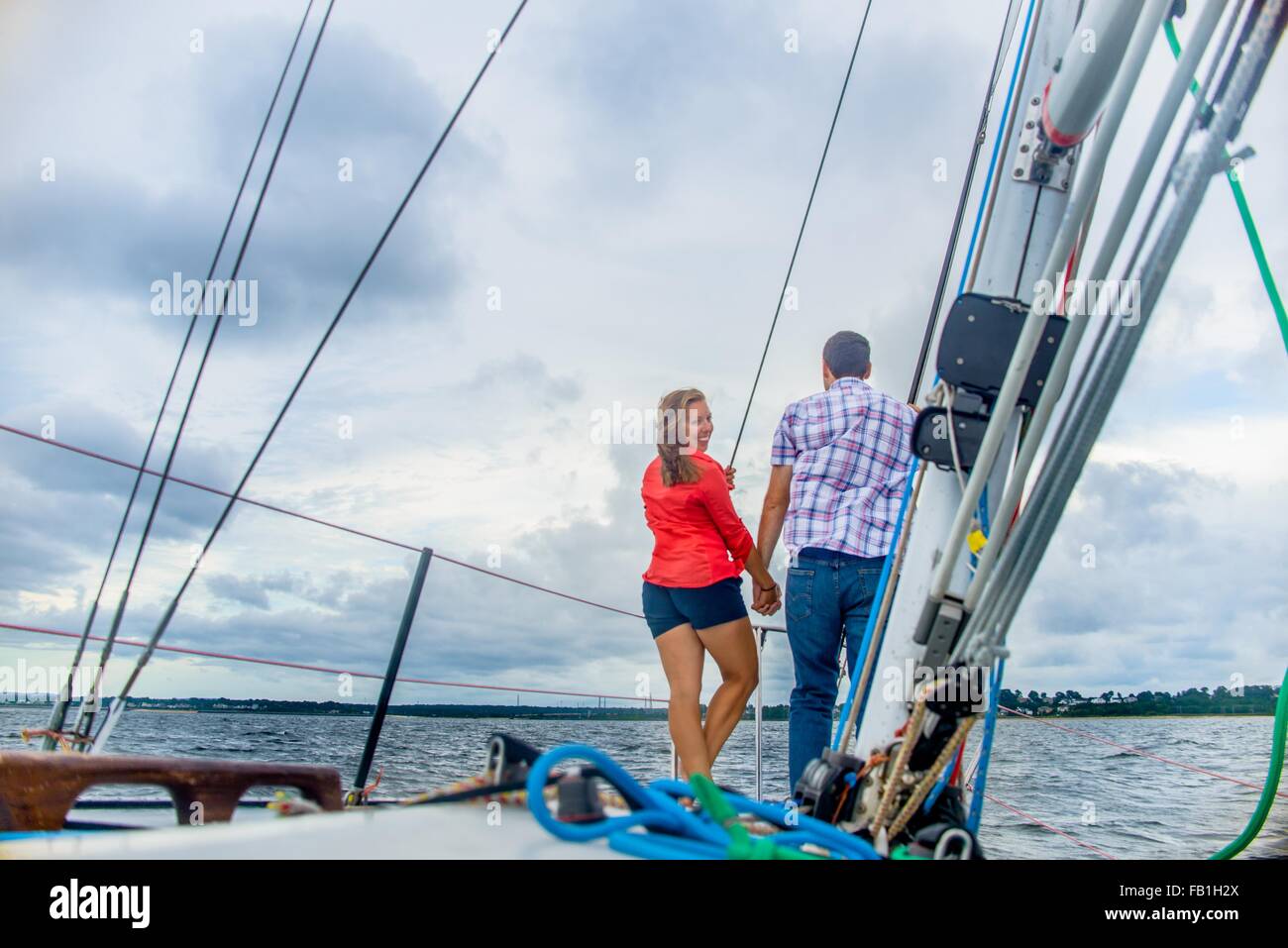 Rear view of couple on bow of boat holding hands, looking over shoulder ...