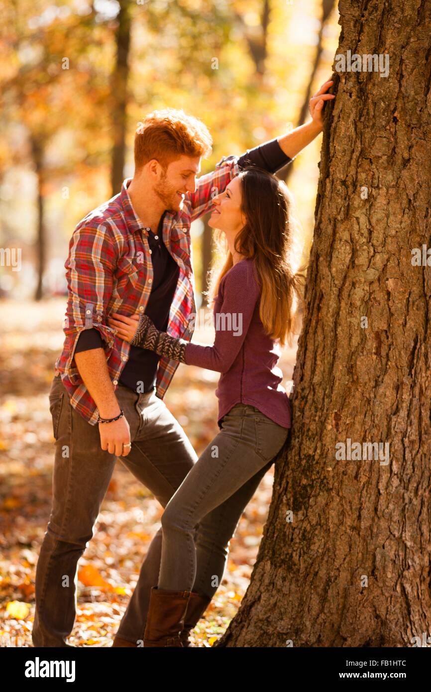Romantic young couple leaning against tree in autumn forest Stock Photo ...