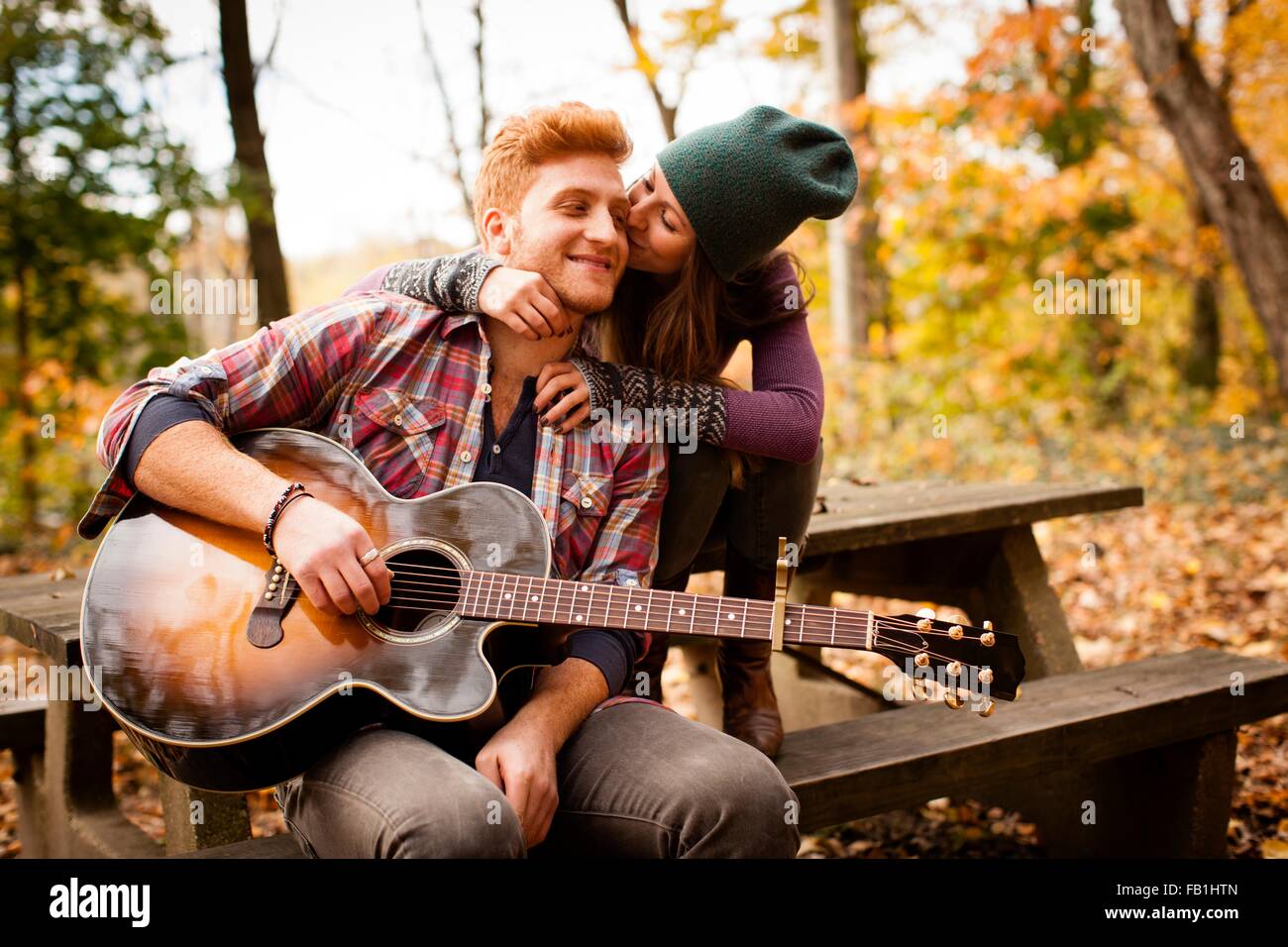 Romantic young couple playing guitar on picnic bench in autumn forest ...