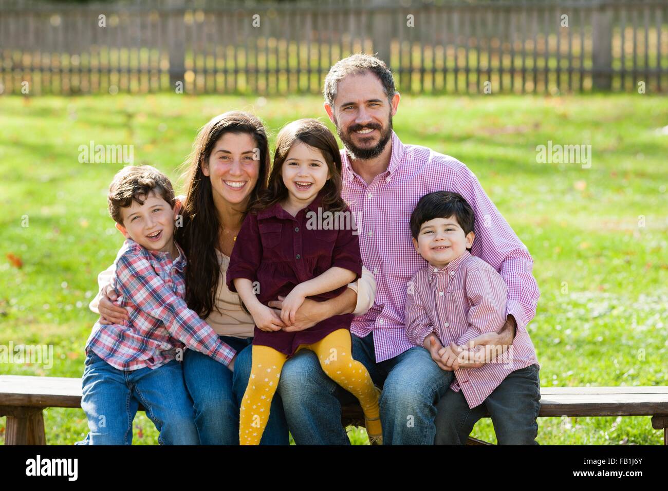 Family sitting on bench together looking at camera smiling Stock Photo ...