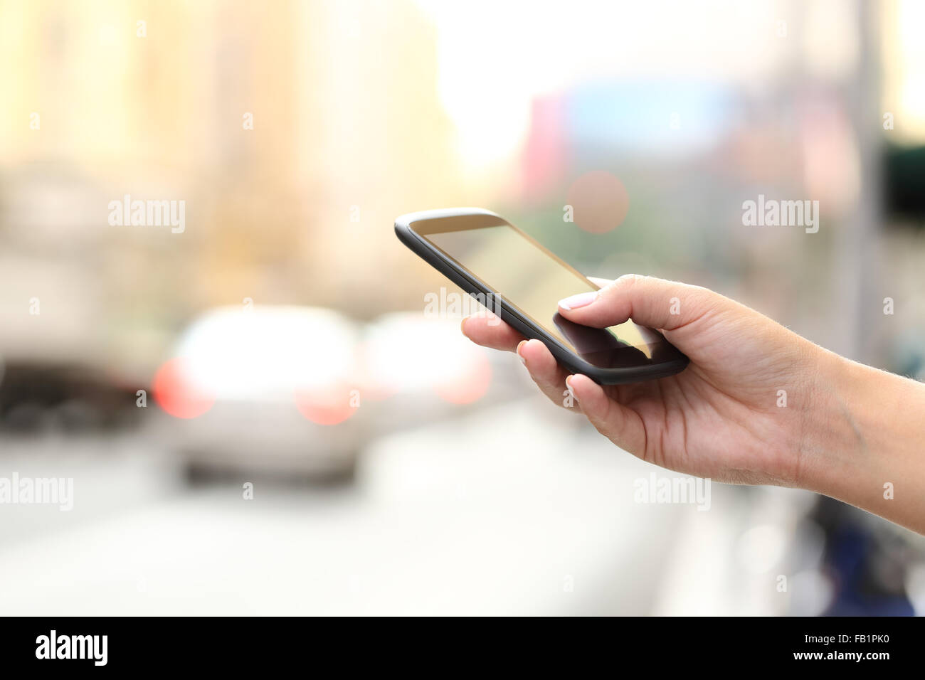 Woman hand texting on a smartphone in the street with an unfocused ...