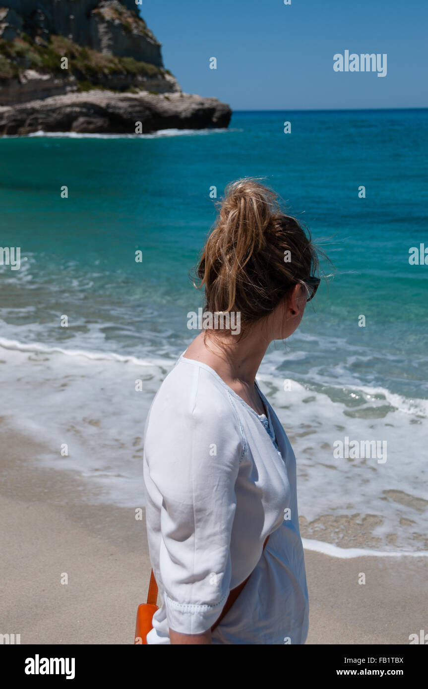 Blond young woman standing at the beach and watching ocean in Tropea ...