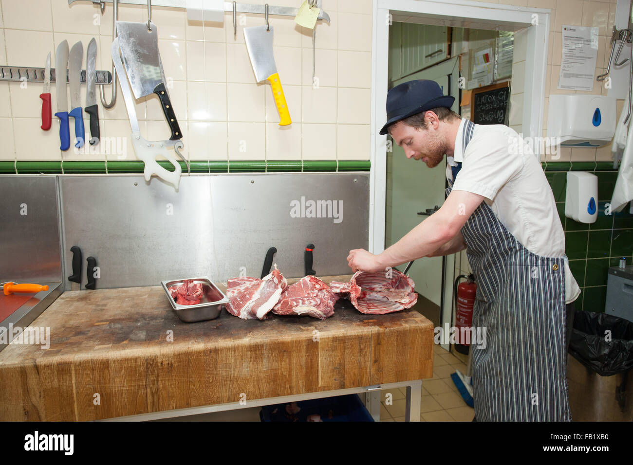 A butcher working in a shop on a butcher board preparing meat for sale ...