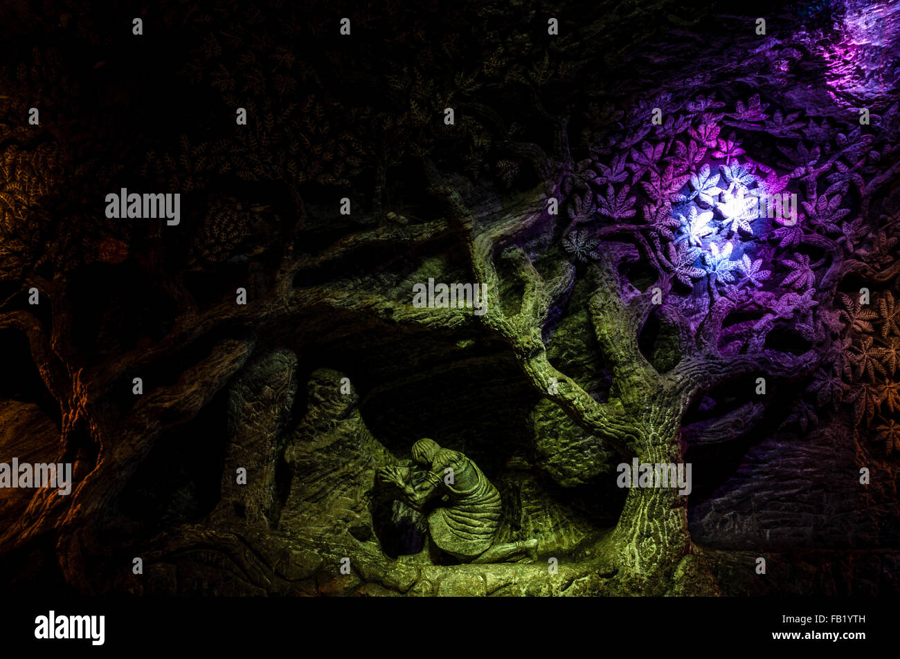 Stone sculpture of a man and tree in purple green light at the ...