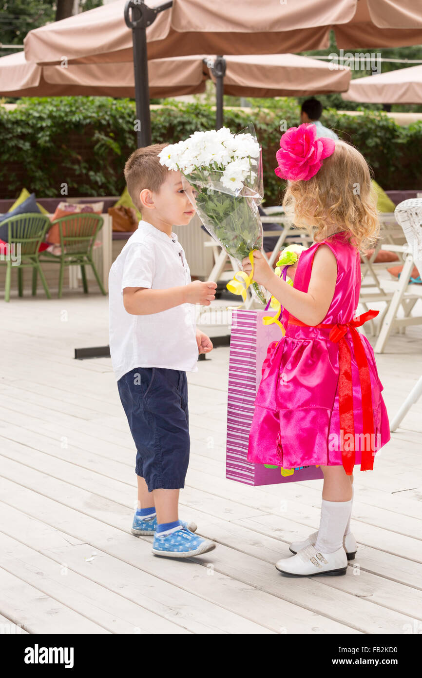 The boy kid gives flowers to girl child on birthday. Little adorable ...
