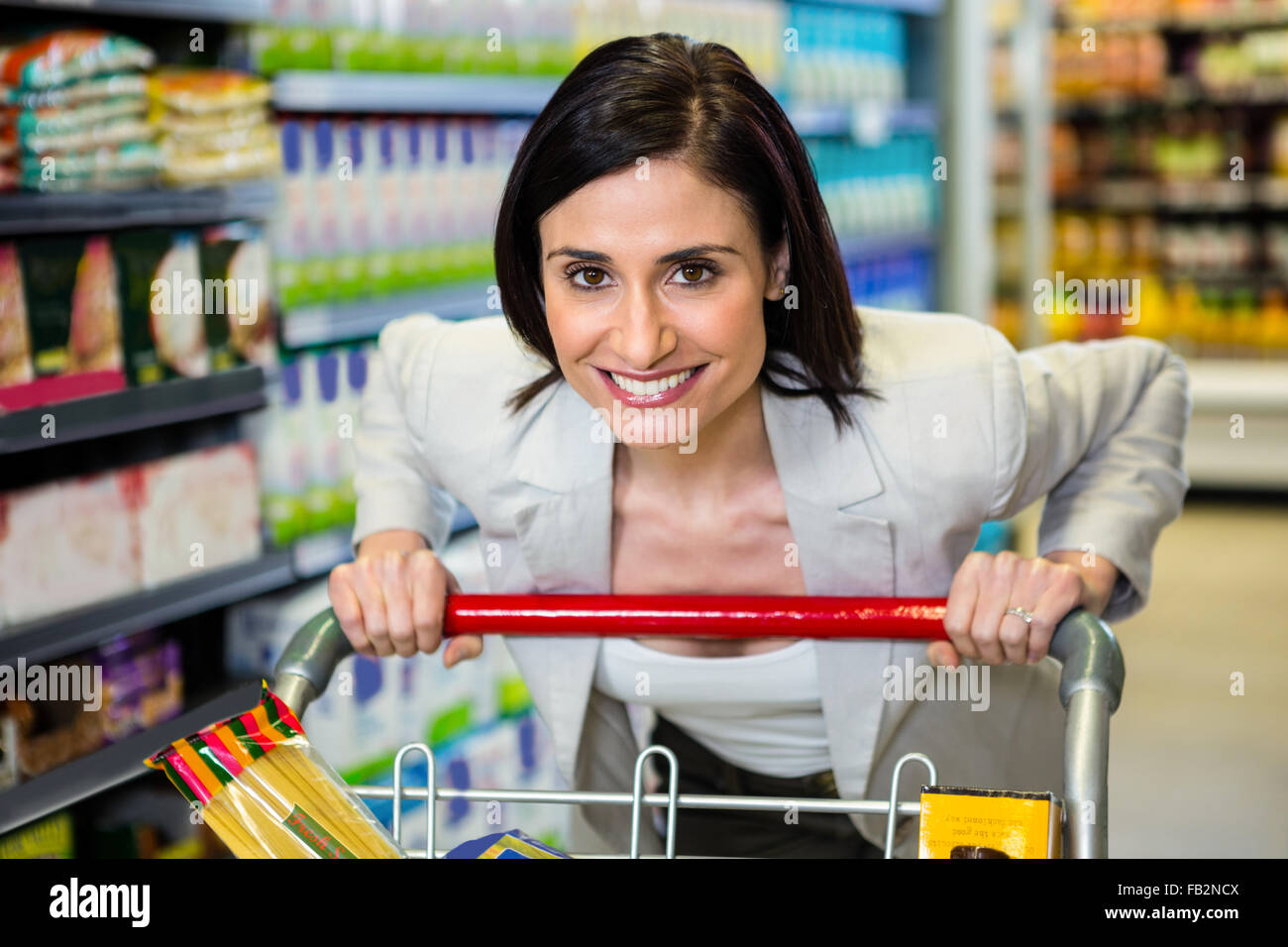 Smiling woman pushing trolley in aisle Stock Photo - Alamy