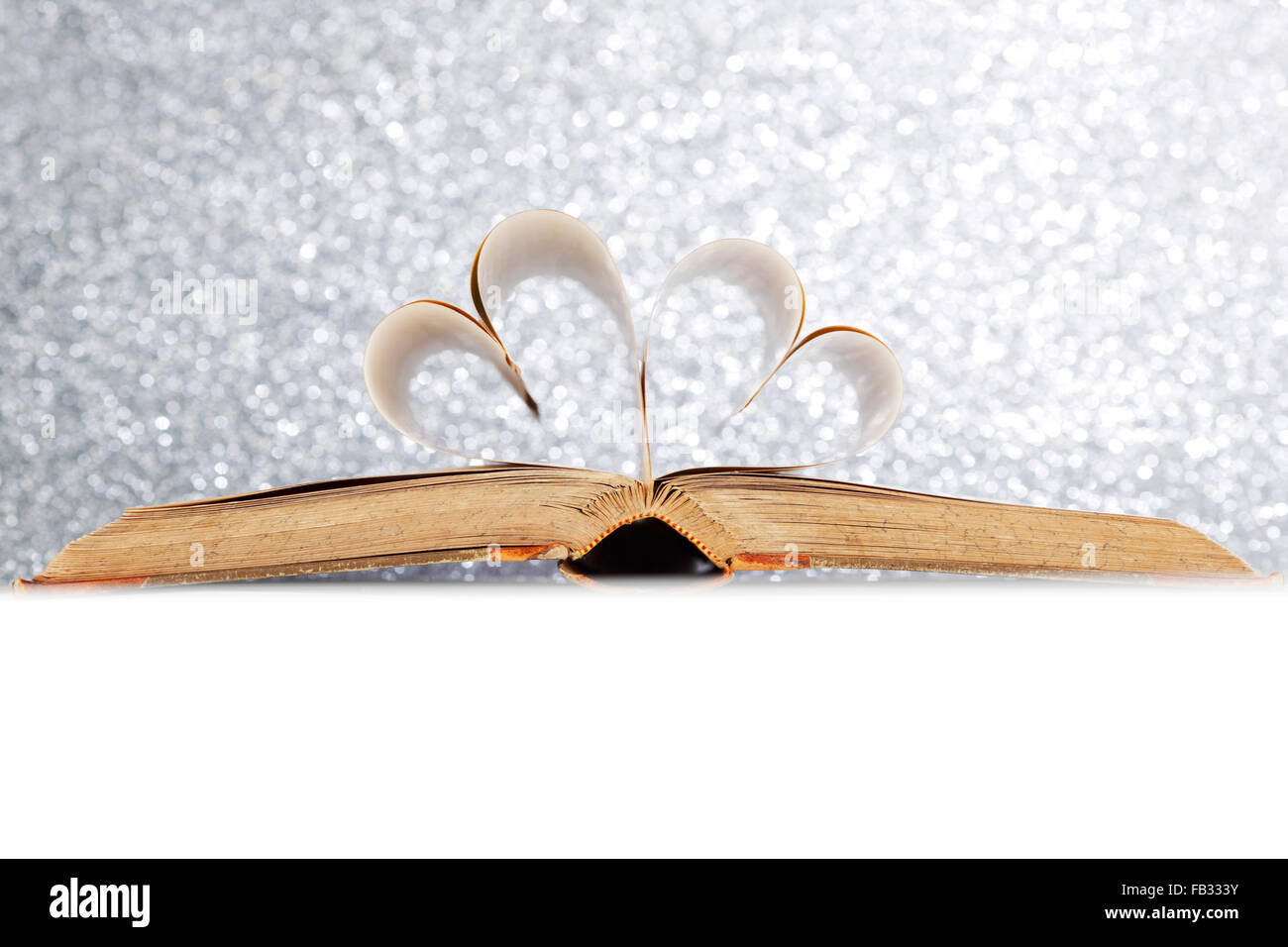 Pages of open book rolled in heart shape on glitter background Stock ...