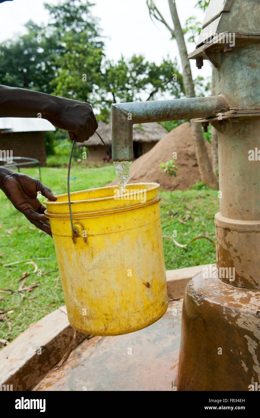 Woman filling bucket with clear water at a hand pump well in the middle ...