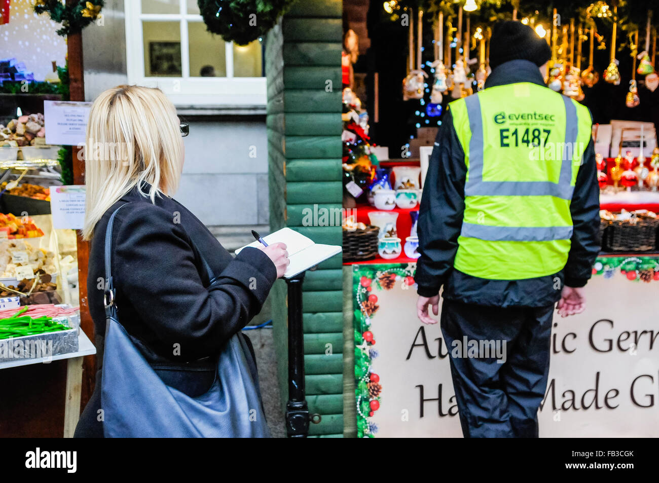 A journalist takes notes at a market, while looking at a security guard ...