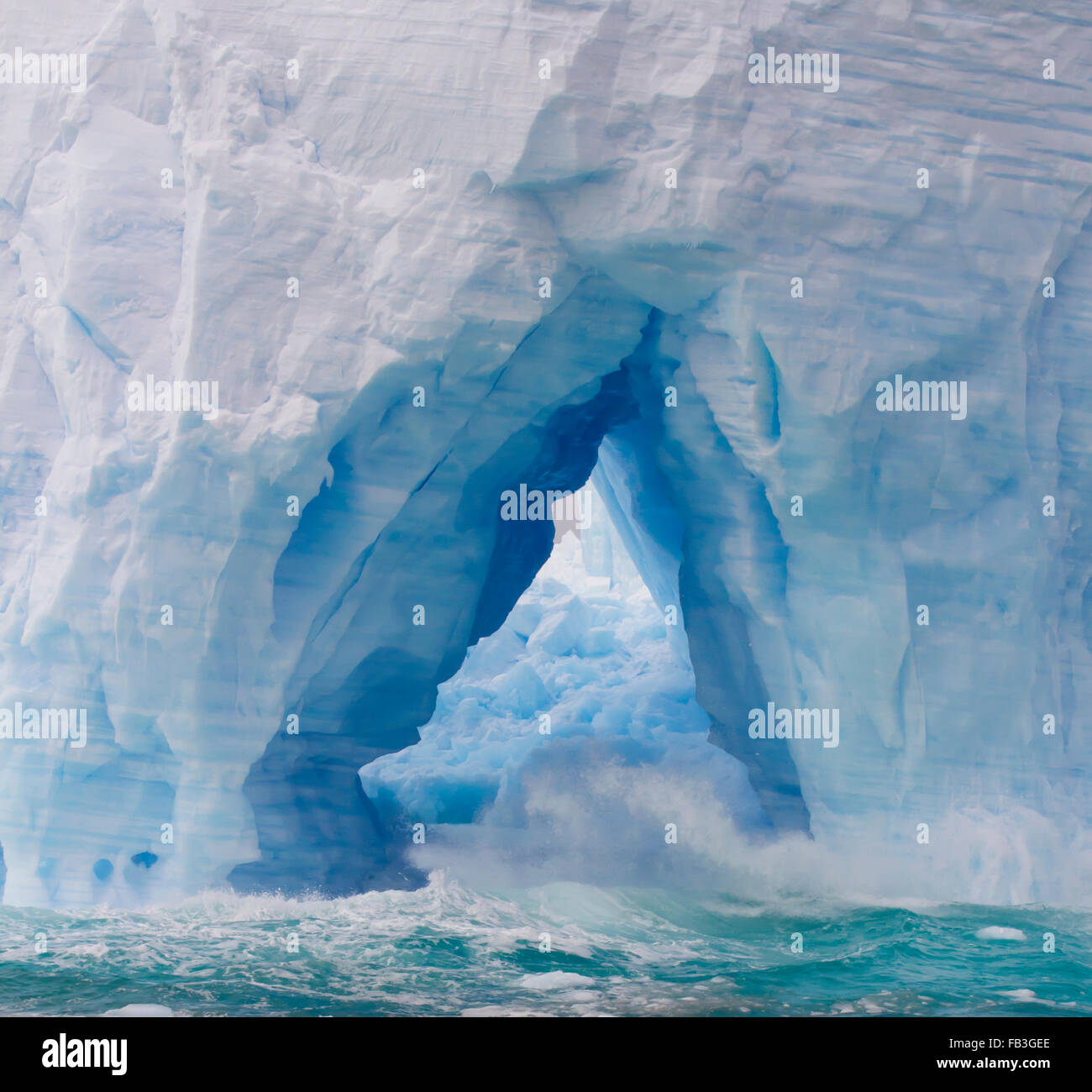 Waves splashing through arches in floating glacial iceberg in ...