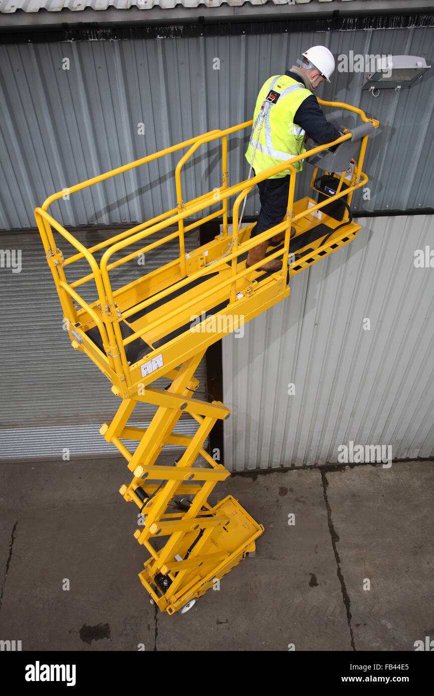 A worker uses a small industrial scissor lift to gain high level access ...