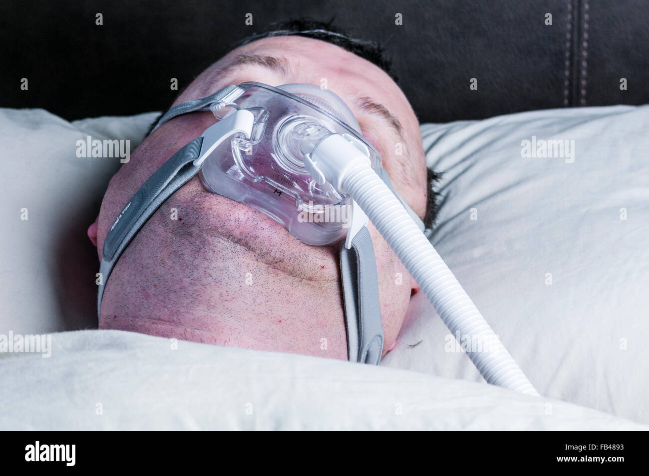 A middle-aged, overweight man wearing a CPAP mask while sleeping in bed ...
