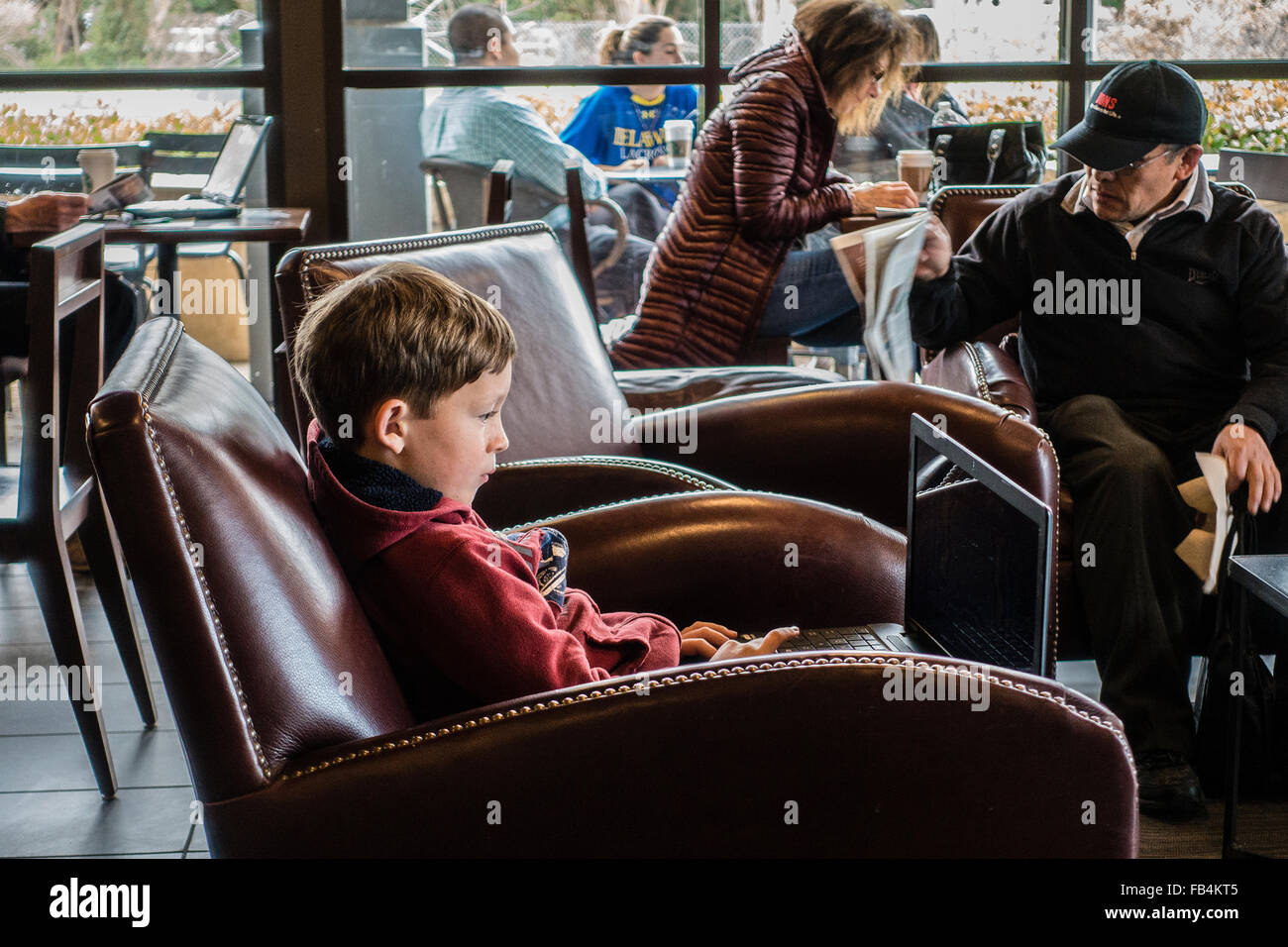 A young technically savvy boy, 10-12 years old, sits in a coffee shop ...