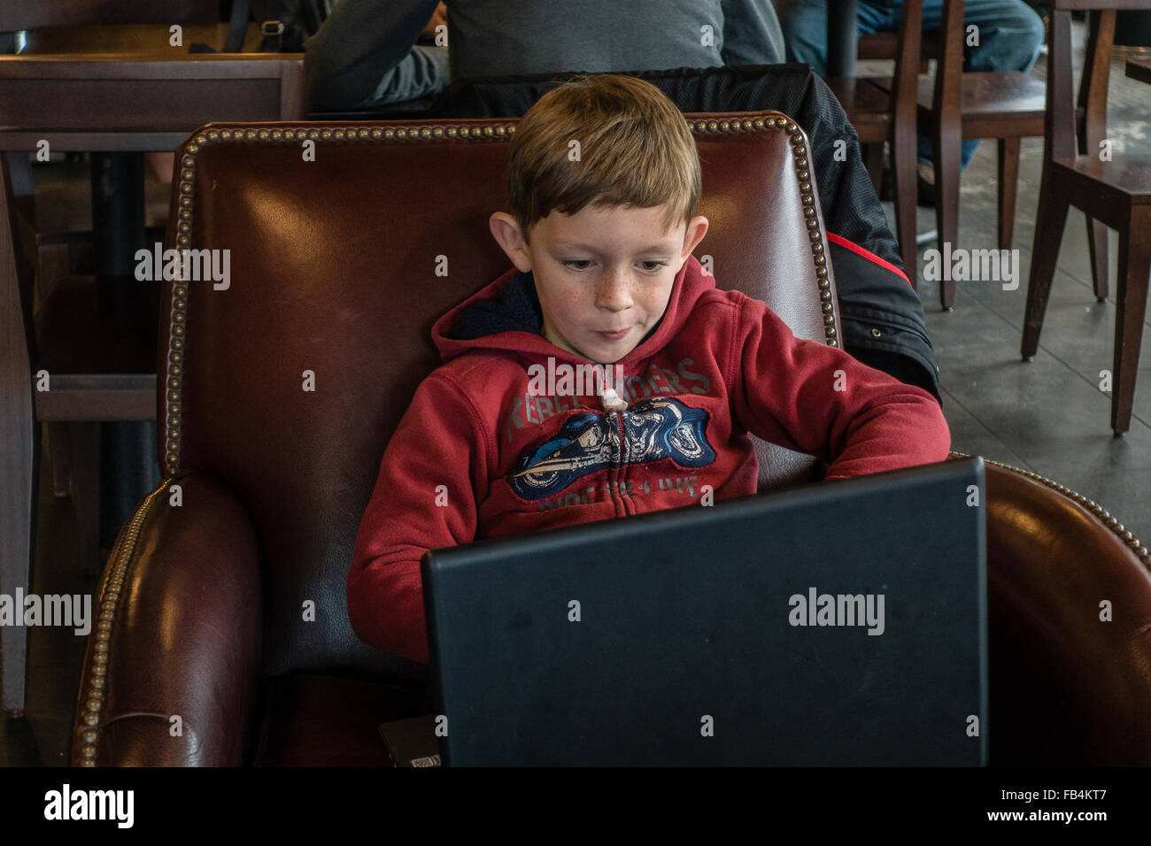 A young technically savvy boy, 10-12 years old, sits in a coffee shop ...