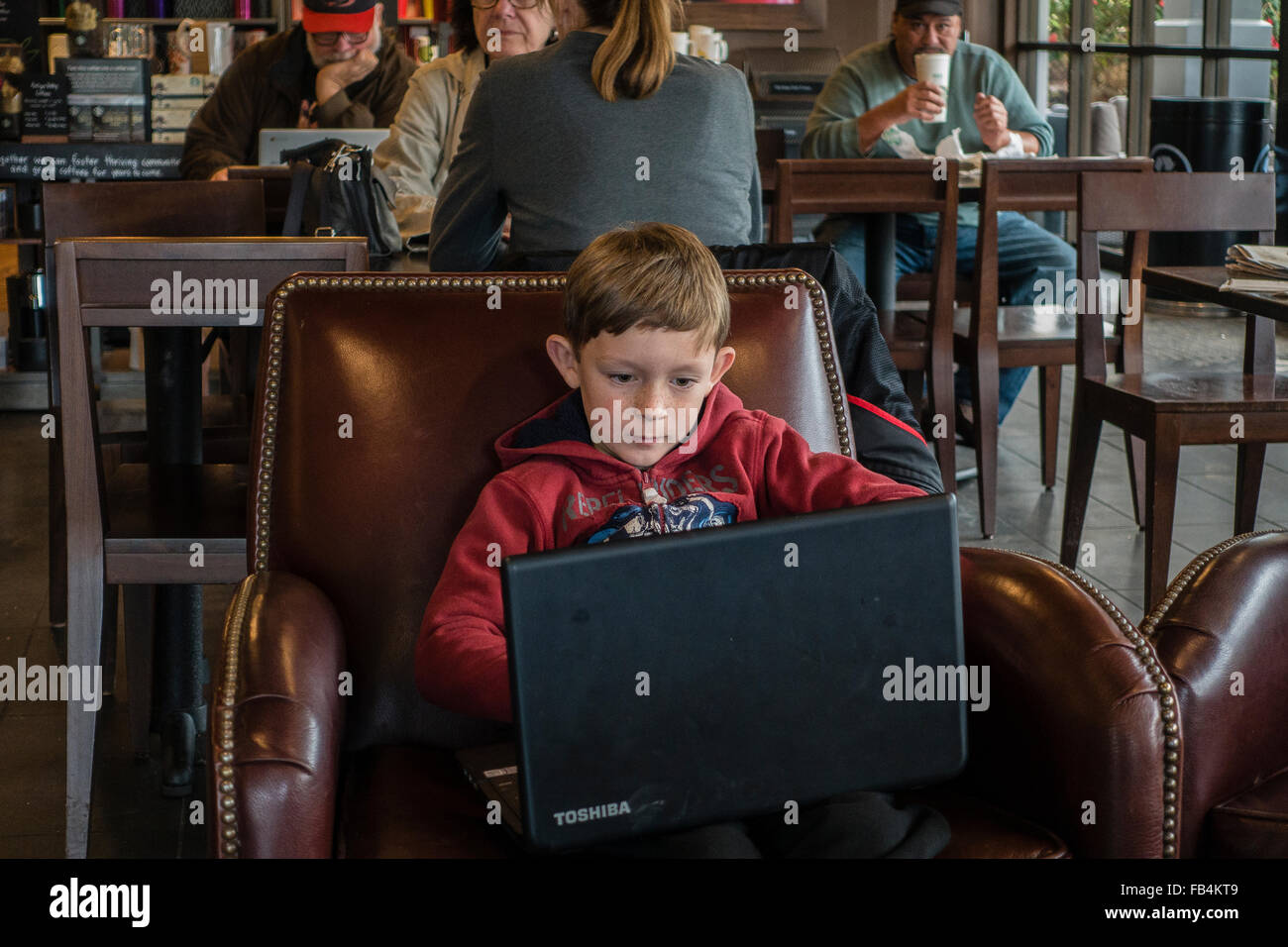 A young technically savvy boy, 10-12 years old, sits in a coffee shop ...