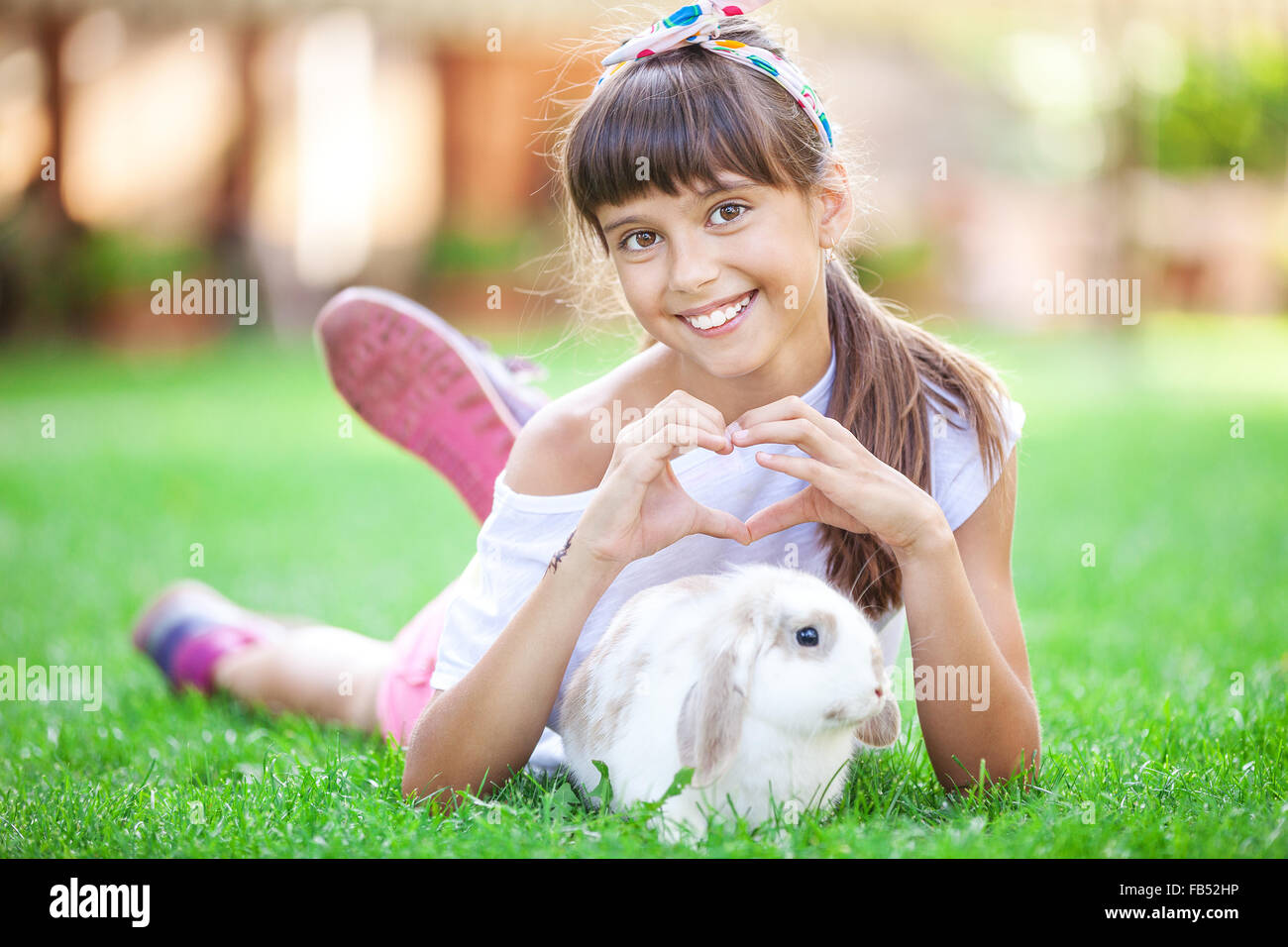 Smiling girl showing a heart sign with her hands over a pet rabbit ...
