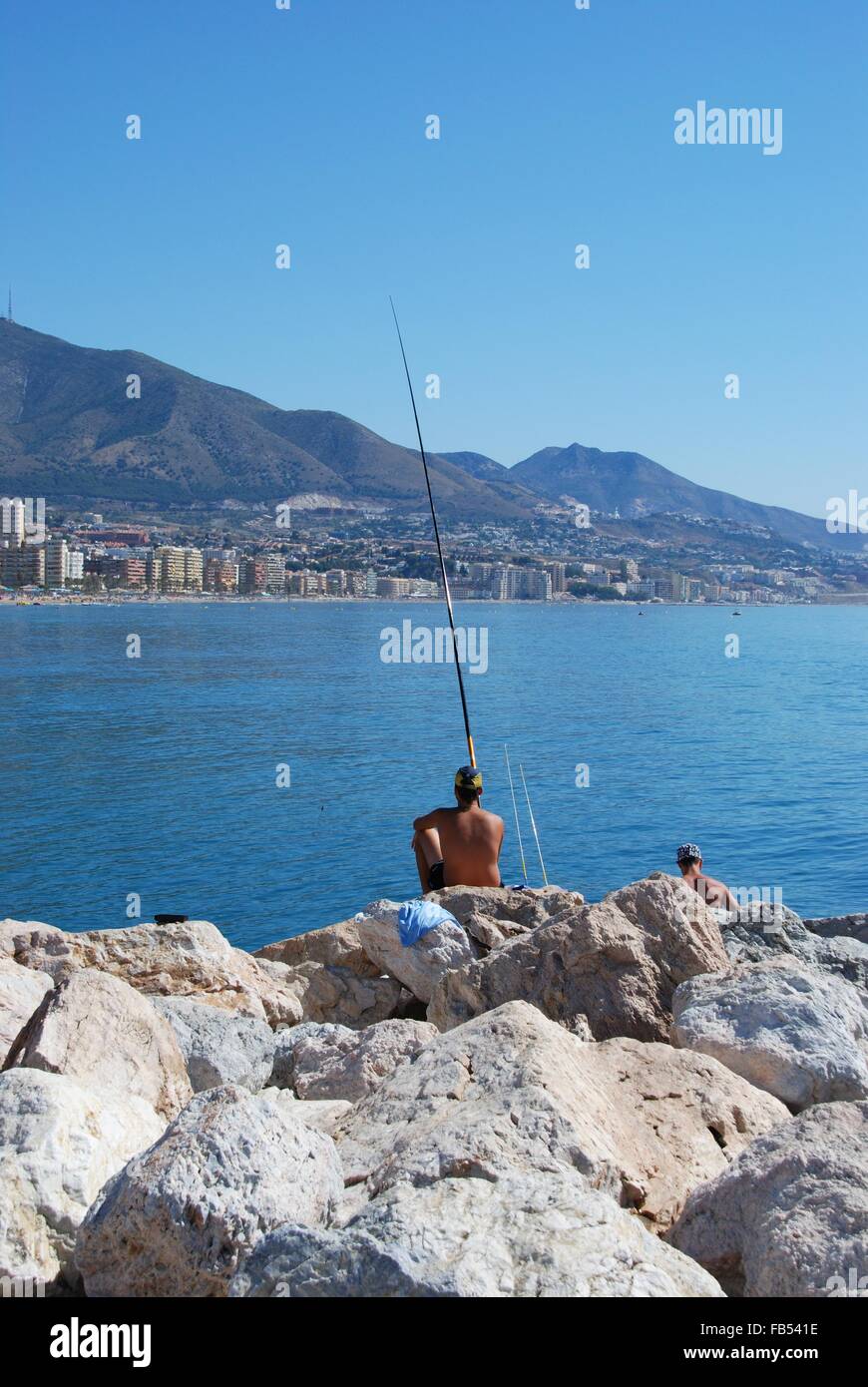 Men fishing from the rocks with views towards the beach and town ...