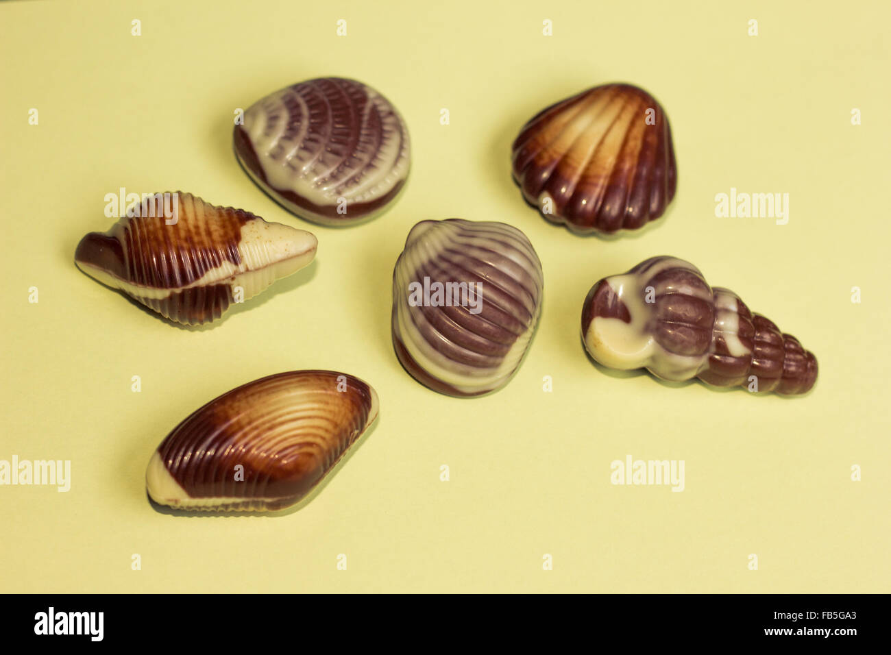 An assortment of Belgian chocolate shells on a yellow/ pale yellow ...