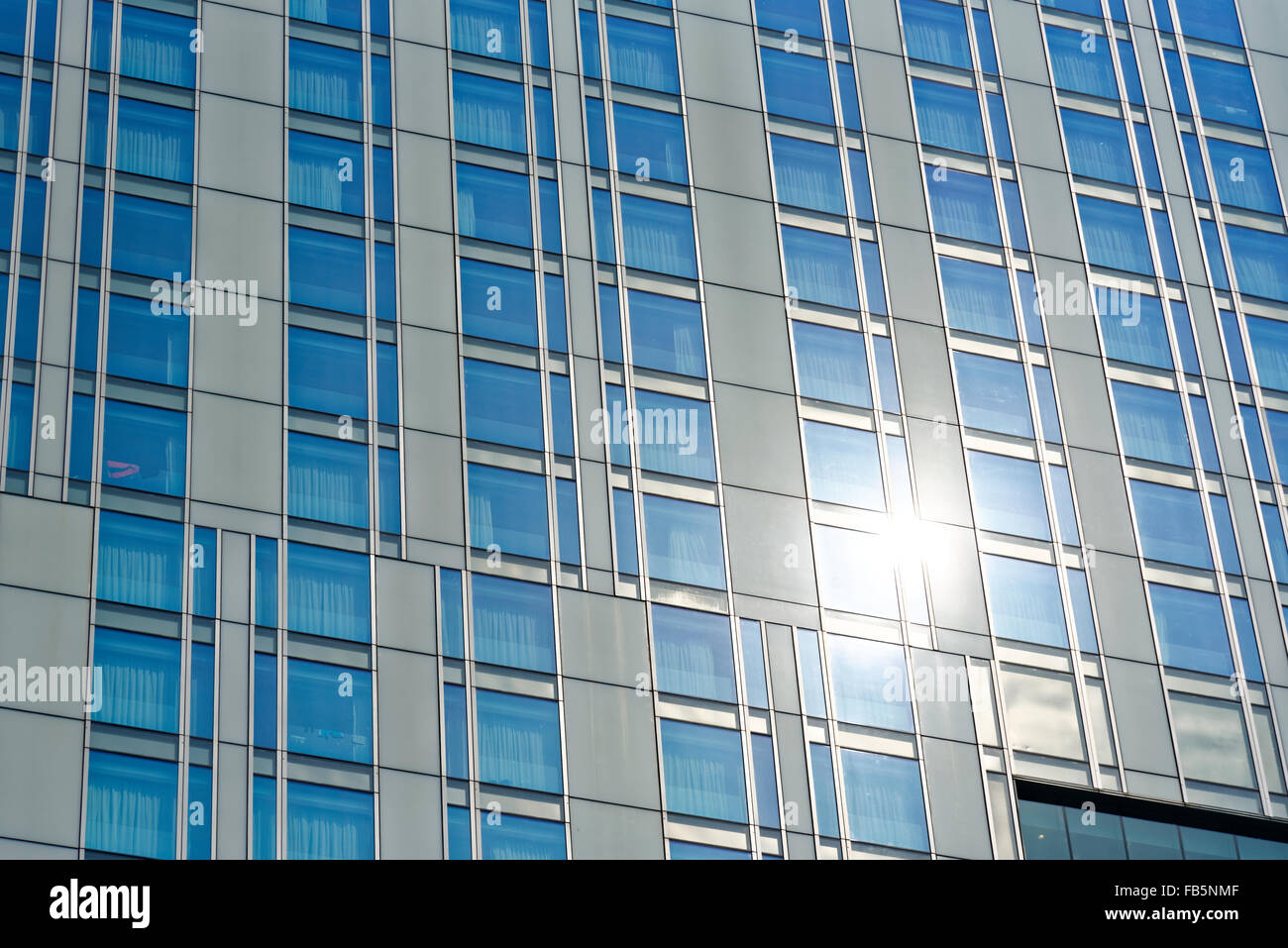 grey Skyscraper with blue windows and a sun flare and blues sky Stock ...