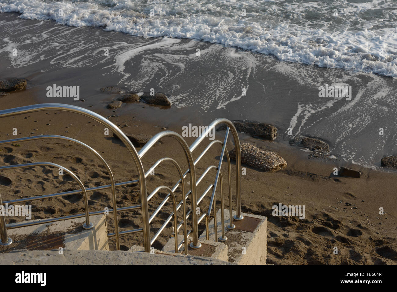 Shiny metal handrail of beach stair on background of sand and splashing ...