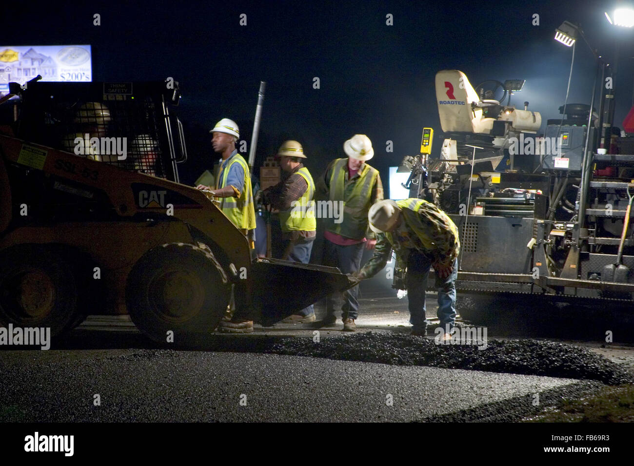 Workers stand behind an asphalt spreader placing hot mix during ...